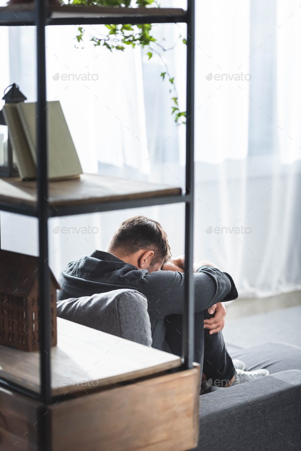 back view of man with panic attack crying and hugging legs in apartment ...