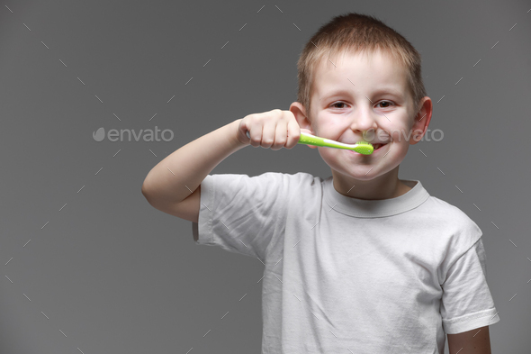 Happy child kid boy brushing teeth with toothbrush on gray background ...
