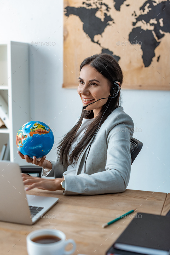 smiling travel agent holding globe while sitting at workplace Stock ...