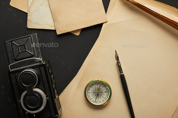 top view of vintage camera, paper, fountain pen, compass on black ...