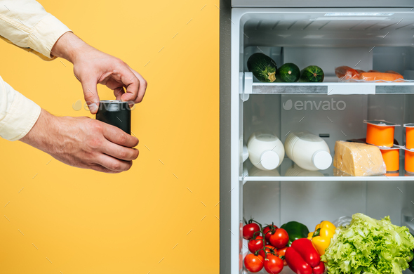 cropped view of man opening can with soda near open fridge with fresh ...
