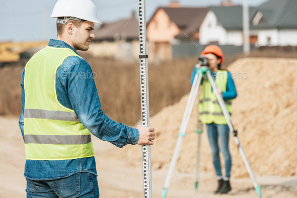 Selective focus of surveyor with ruler and colleague with digital level ...