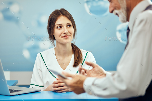 Smiling nurse communicating with a patient at reception desk at medical ...
