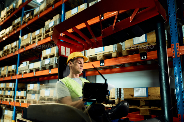 Forklift operator going through paperwork while working in a warehouse ...