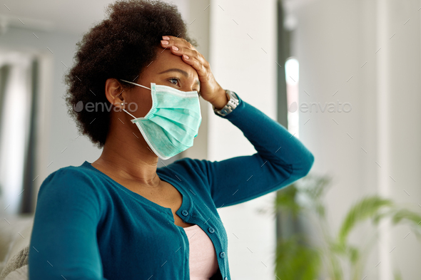 Distraught African American woman with face mask holding her head in ...