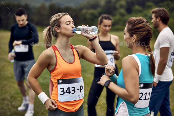 Marathon runner drinking water while talking to her friend in nature ...