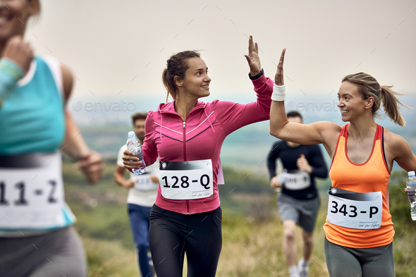 Happy athletic women running a marathon and giving high-five to each ...