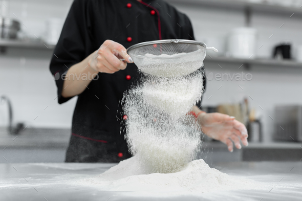 The pastry chef's hands sift the flour through a sieve on the table ...