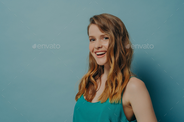 Positive millenial girl with wavy hair stands sideways and looks at ...