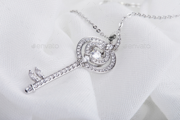 Gold pendant in the shape of a key with precious stones on white airy ...