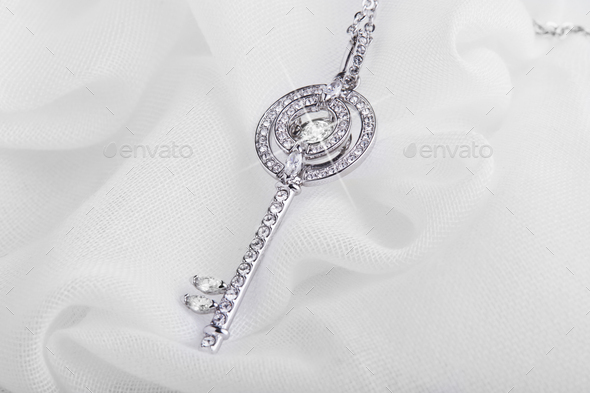 Gold pendant in the shape of a key with precious stones on white airy ...