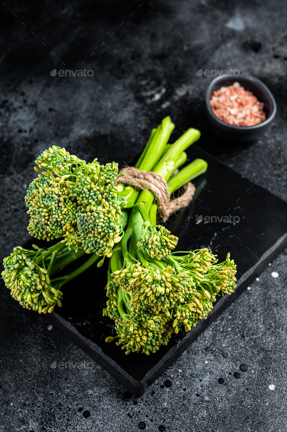 Raw green Broccolini branch on a marble board. Black background. Top ...