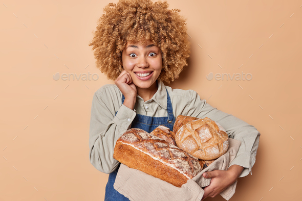 Positive female baker with curly hair smiles happily poses with various ...