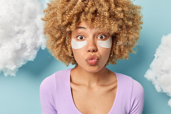 Headshot of curly haired woman keeps lips folded looks surprisingly at ...