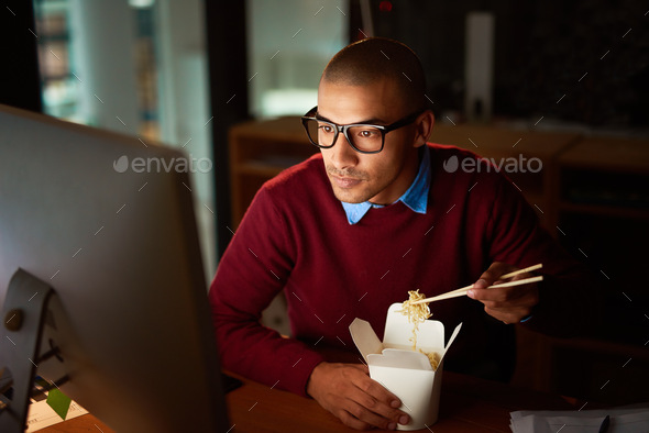Shot of a handsome young man eating Chinese food while working late in ...