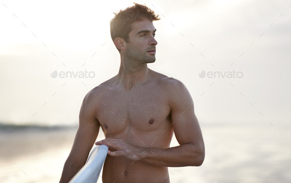 Chasing waves is his passion. A handsome young surfer at the beach ...