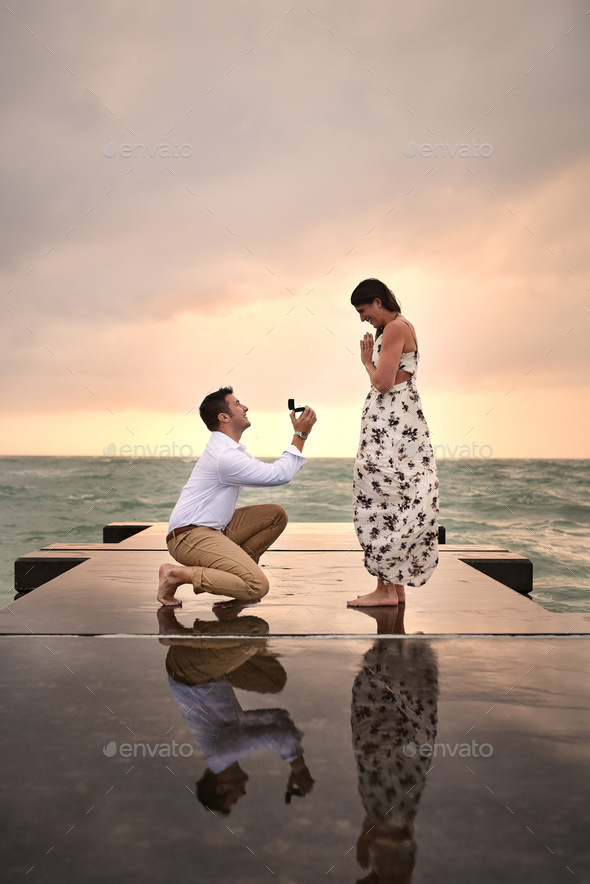 Full length shot of a handsome young man proposing to his girlfriend on ...