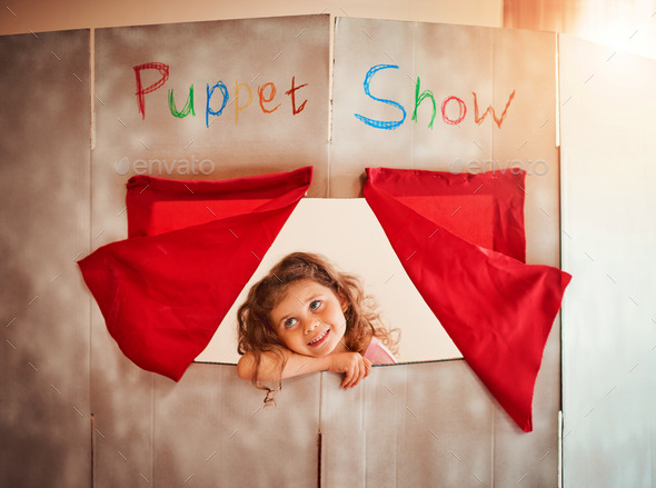 Shot of an adorable little girl standing in the window of a puppet show ...