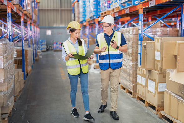 2 Staff in large depot storage warehouse manager and trainee walking ...