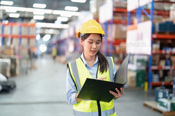 Staff working in large depot storage warehouse hold check list walking ...