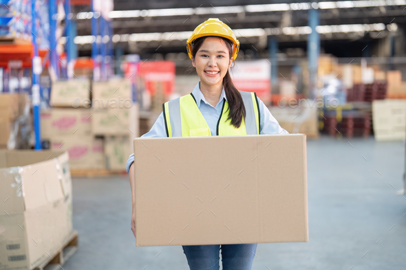 Staff working in large depot storage warehouse lift up heavy carton box ...