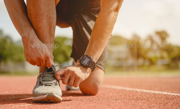 The young man are using their hands to tie their shoes for jogging on ...