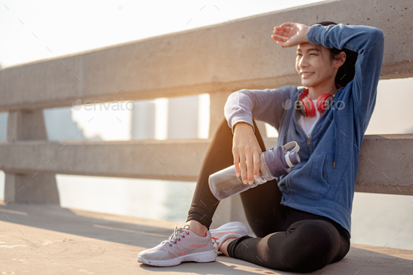 Young woman drink water and sitting to rest after jogging a morning ...