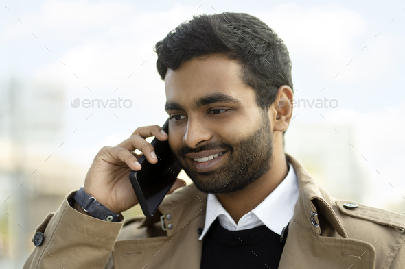 Handsome smiling Indian man talking on mobile phone on the street ...