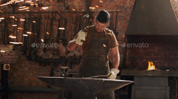 Shot of a metal worker hitting a hot metal rod with a hammer in a ...