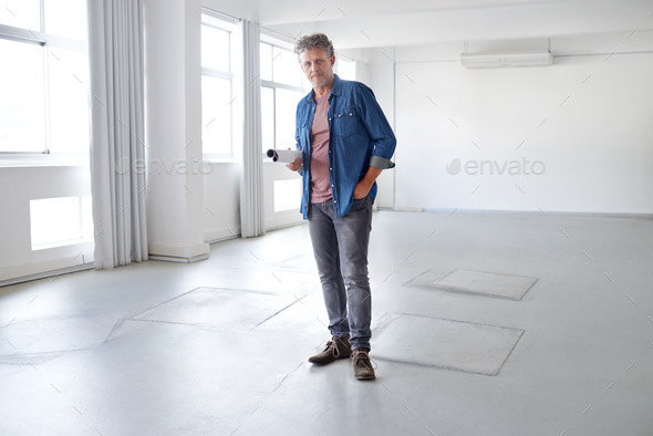 A portrait of a mature man standing in an empty room holding building ...