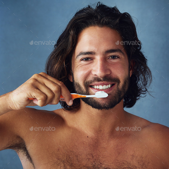Studio portrait of a handsome young man brushing his teeth against a ...