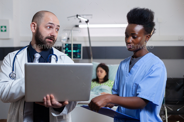 Practitioner doctor with black medical nurse assistant checking ...