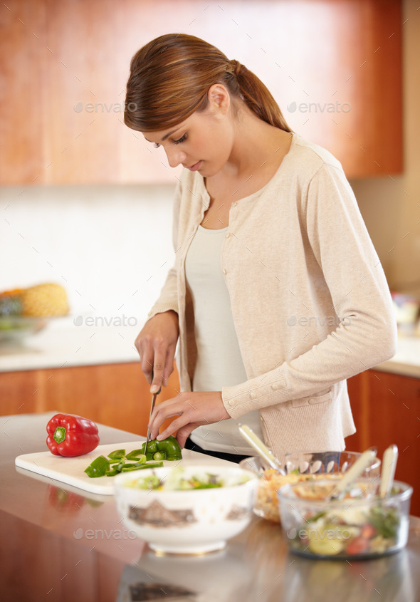 Preparing a meal. An attractive young woman cooking in the kitchen ...