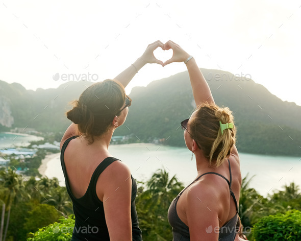 Shot of two friends making a heart shape with their hands while on ...