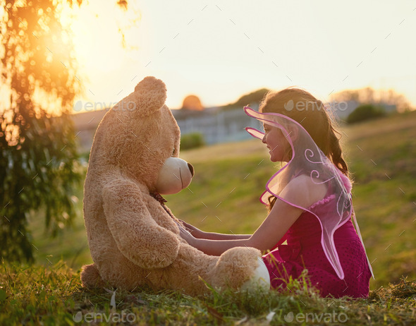Fun in the park with Ted. Shot of a cute little girl playing with a huge teddybear in the park ...