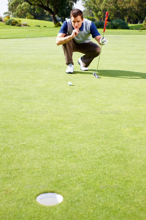 Full length of man crouching on the putting green and assessing his ...