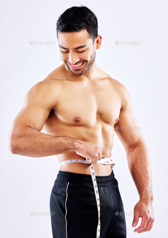 Shot of a male athlete measuring his waist against a white studio ...