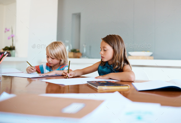 Shot of two adorable young children doing their homework together at ...