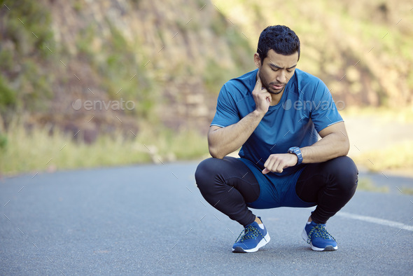 Full length shot of a handsome young man crouching and timing his pulse ...
