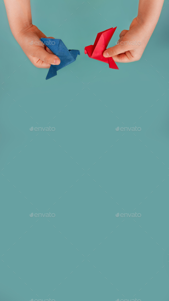 red and blue paper origami pigeons in children's hands on blue ...