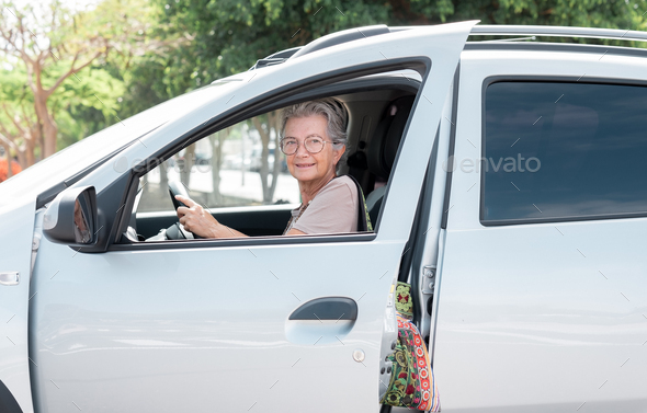 Attractive caucasian senior woman entering in her car, active female ...