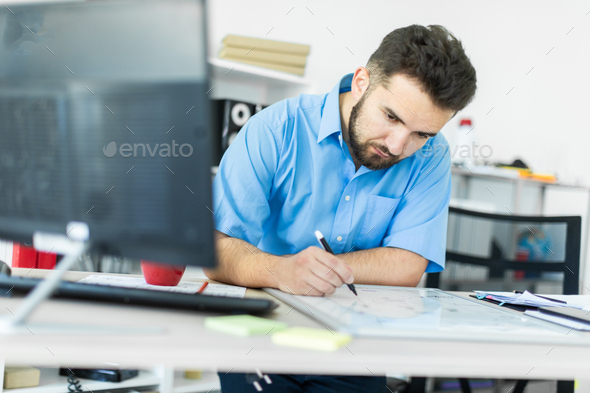 A young man standing in the office at a computer Desk and working with ...