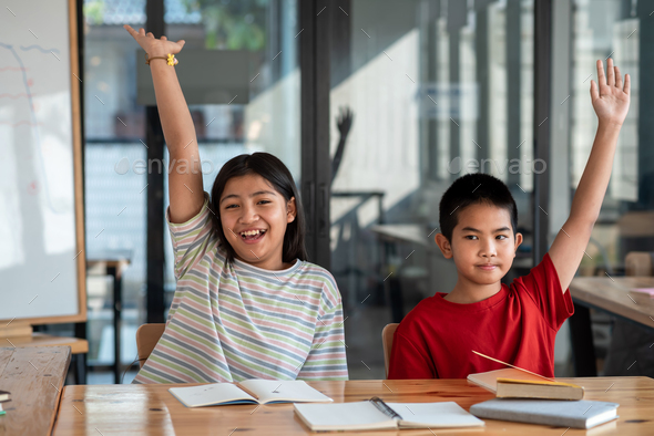 Young Asian man and woman sitting in the classroom raising their hand ...
