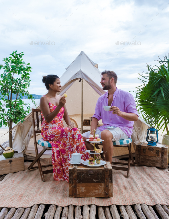 couple having high tea on the beach in front of a tent, men and women ...