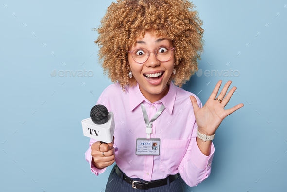 Happy surprised curly female reporter holds microphone keeps palm ...