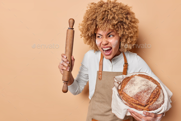 Outraged curly haired female baker smeared with flour screams angrily ...