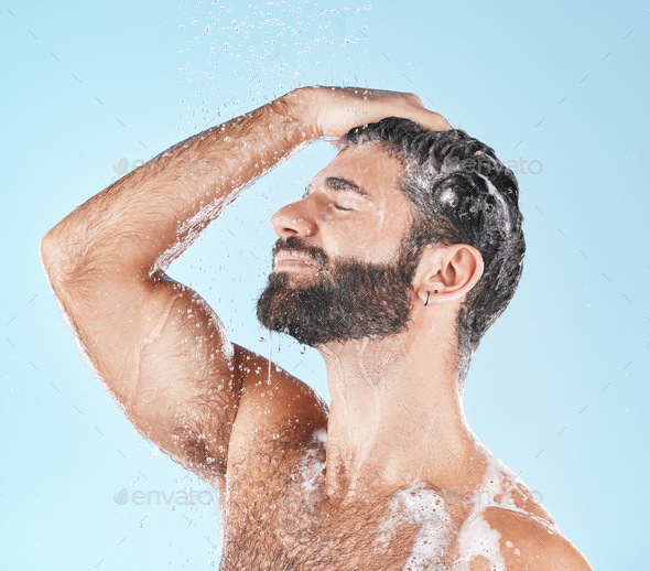 Face, water splash and shampoo shower of man in studio isolated on a blue background. Water ...