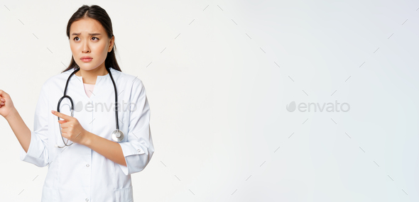 Skeptical female doctor, concerned nurse pointing and looking left with ...