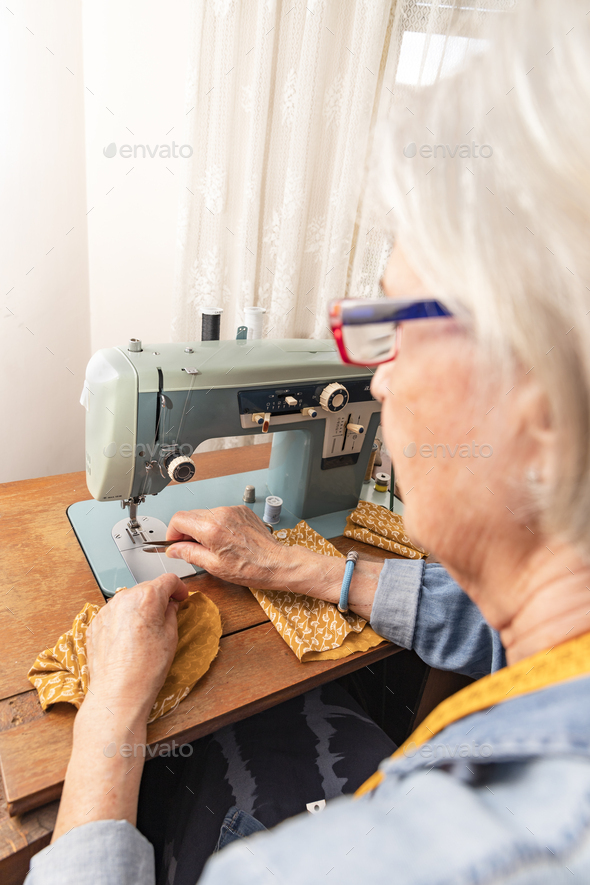 profile of older woman in front of an antique sewing machine cutting a ...