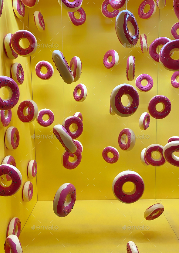 Vertical shot of donut figures hanging from ropes in a yellow room ...